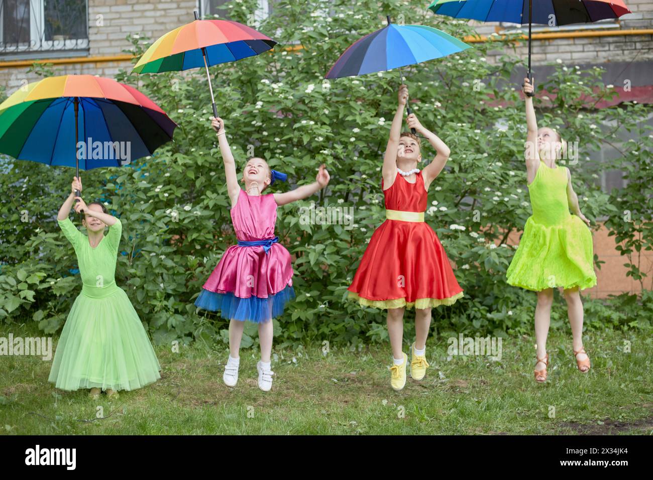 Four girls in dance suits jump throwing up coloured rainbow umbrellas ...