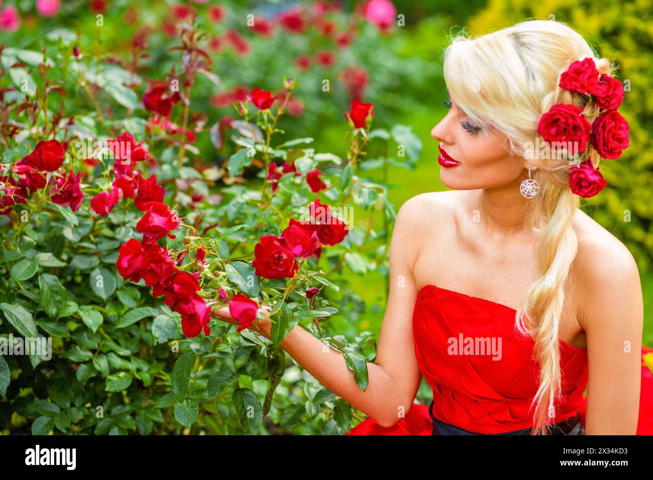 beautiful woman in red dress in park sitting on grass touching flowers ...