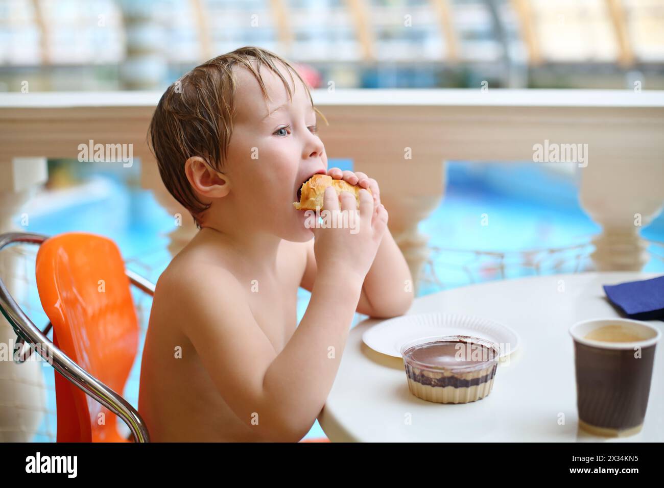 Little boy eating a bun and chocolate pudding in a cafe in the ...