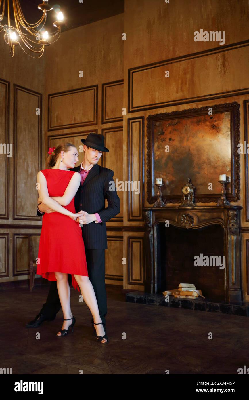 Happy handsome girl and man in black hat dancing tango in retro room ...