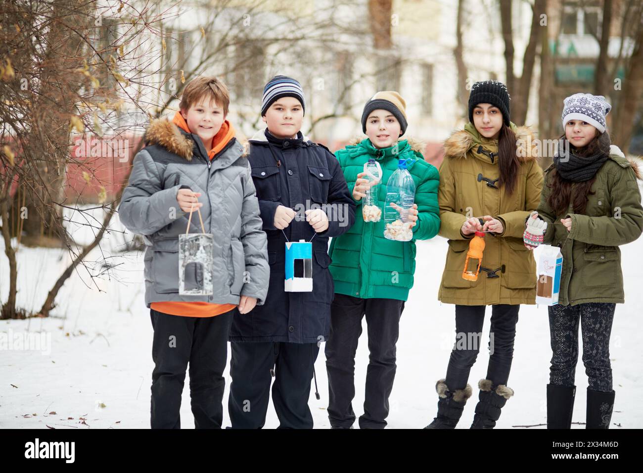 Five children stand together, holding home-made bird feeders with seeds ...
