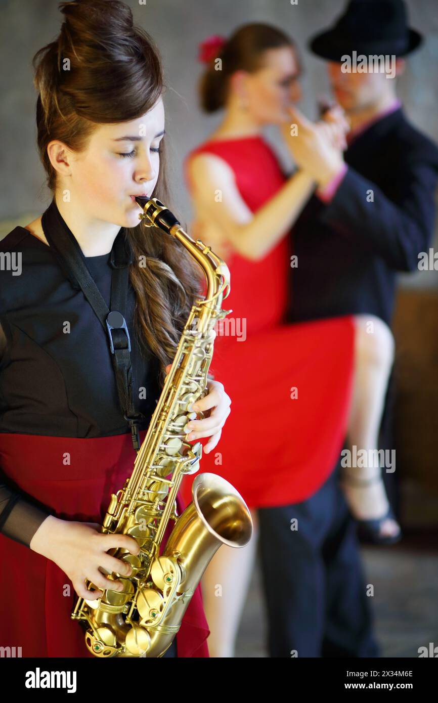 Pretty girl playing saxophone next to dancing pair, focus on musician ...