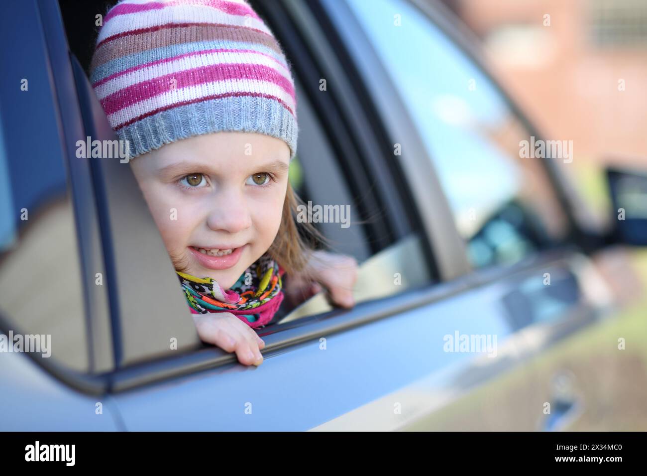 Portrait of little girl in striped hat looking out car window Stock ...