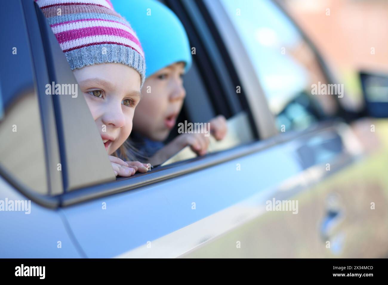 Little girl in striped hat and boy looking out car window Stock Photo ...