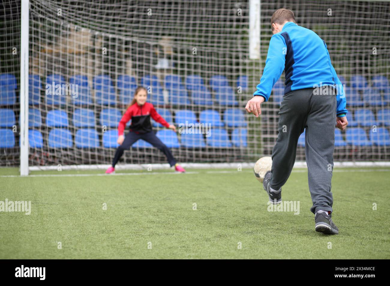Boy in a blue tracksuit throws the ball into the goal with girl keeper ...