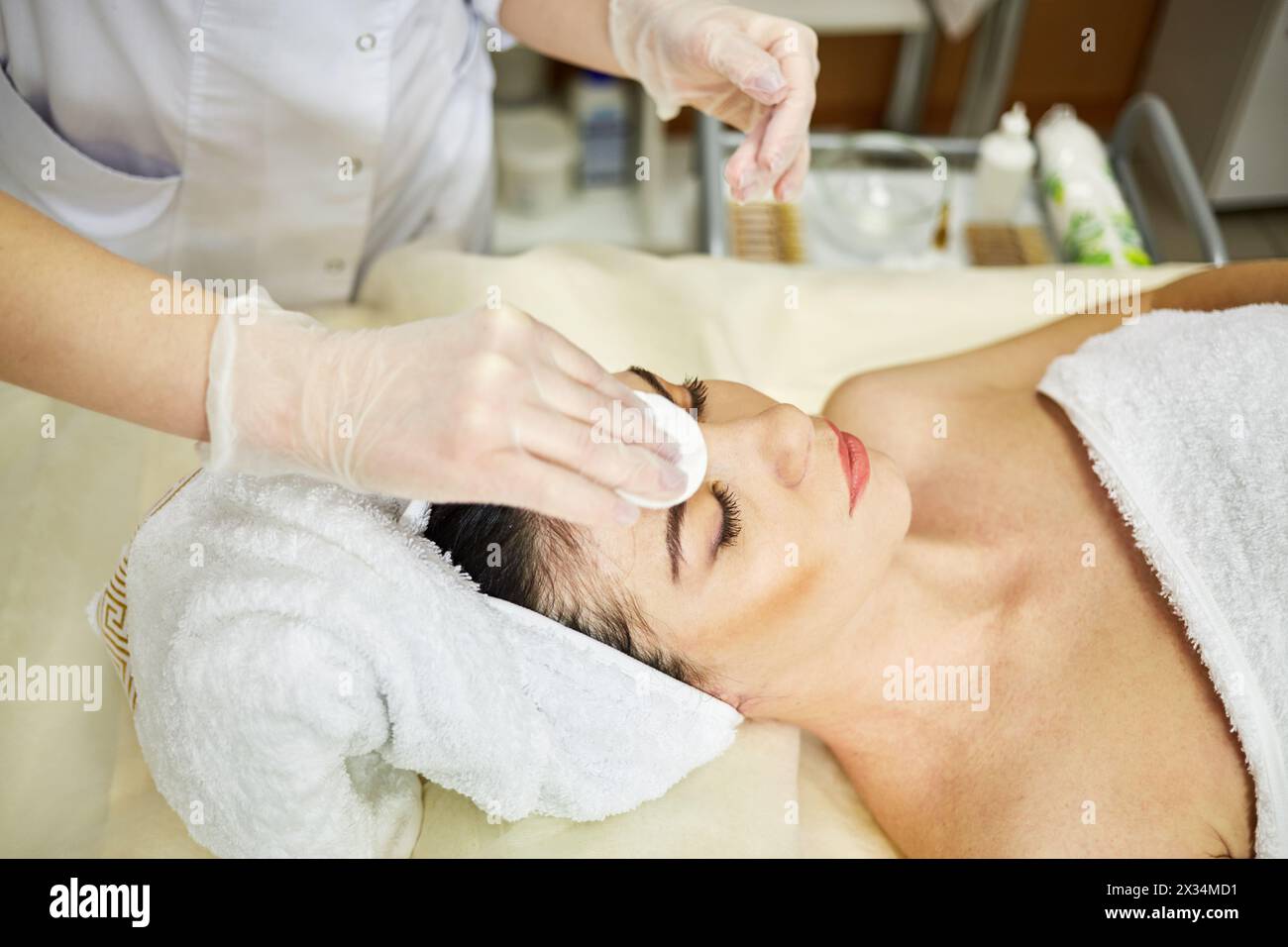 Beautician hands in rubber gloves wipe with cotton pad forehead of ...
