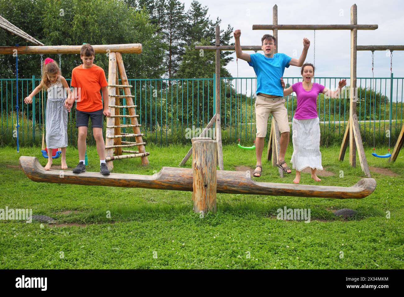 Parents with son and daughter jumping on a swing on a wooden playground ...