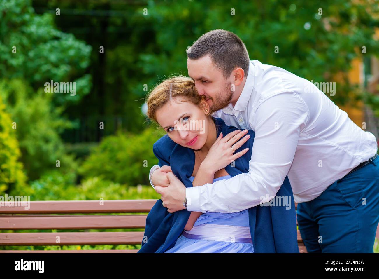 Woman sits on bench, man puts his jacket for girl and hugs she in green ...