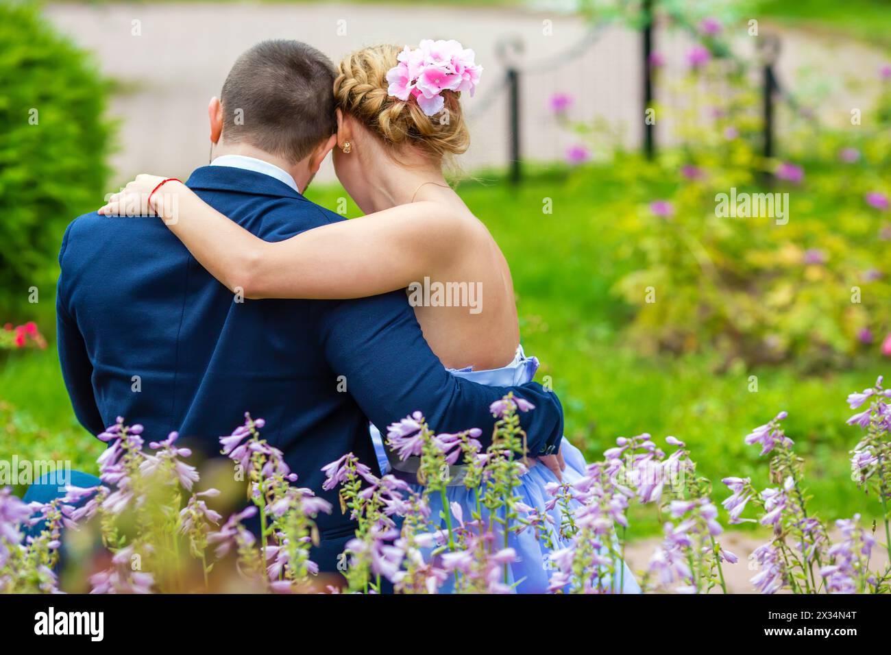 Woman in dress and man in jacket sit on bench and hug in green summer ...