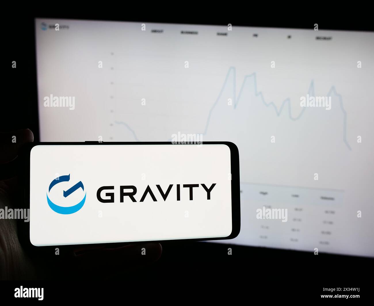 Person holding mobile phone with logo of South Korean video game company Gravity Co. Ltd. in ...