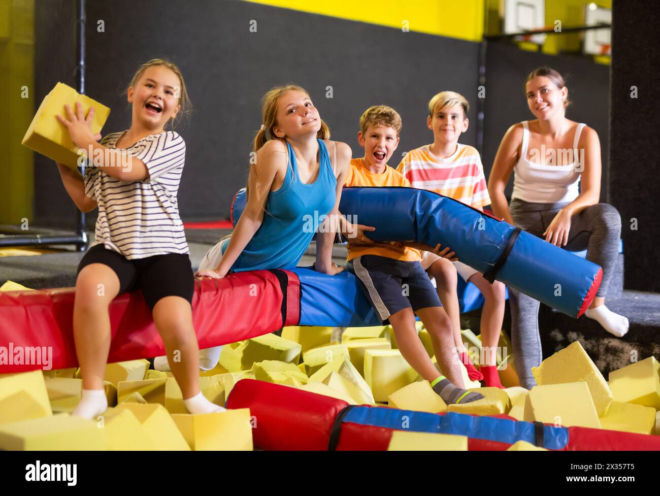 Happy tween children with woman sitting on soft beam above foam pit ...