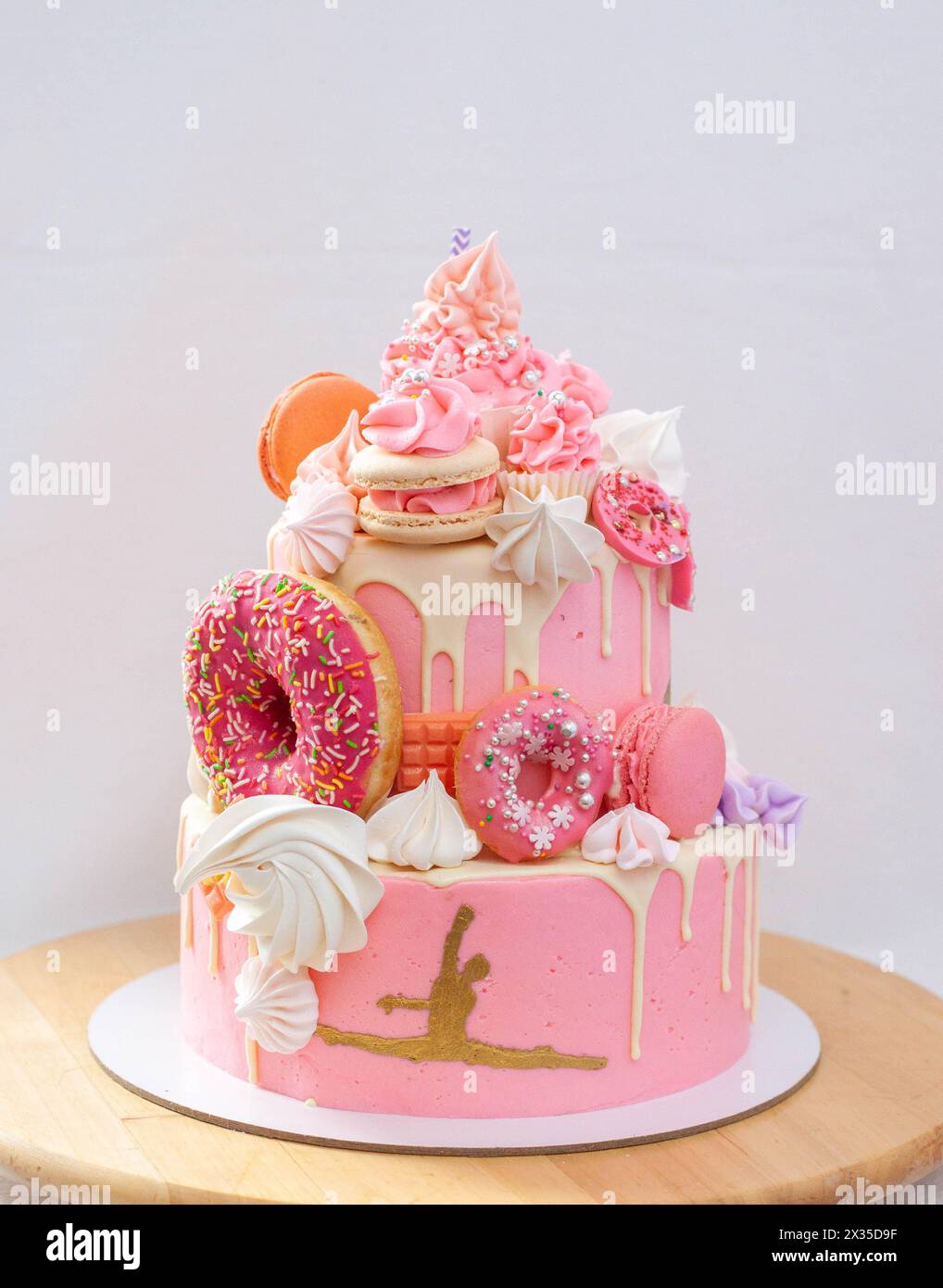 Pink layered tall cake with pink frosting, cake pops, macaroons, meringues, donuts and golden ...