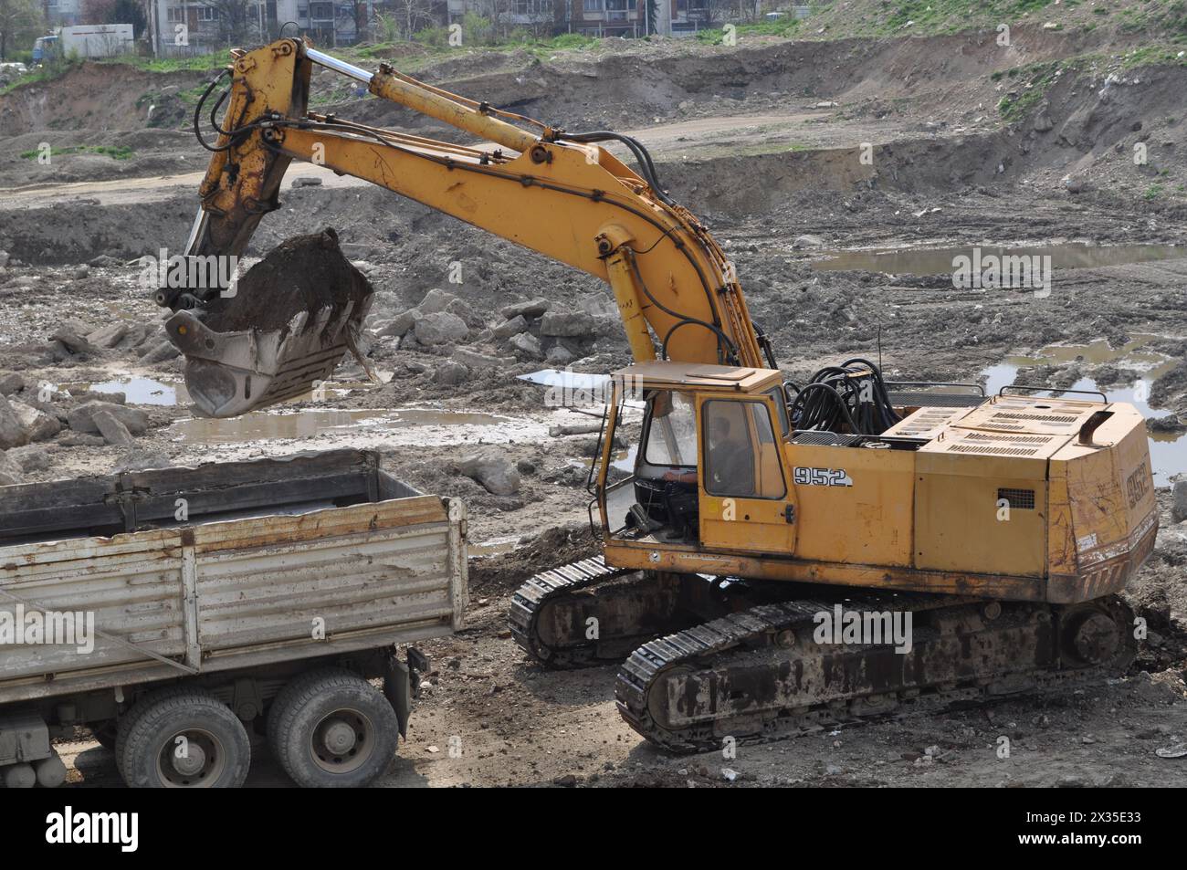 Excavator loads excavated soil into a large truck in a populated area ...