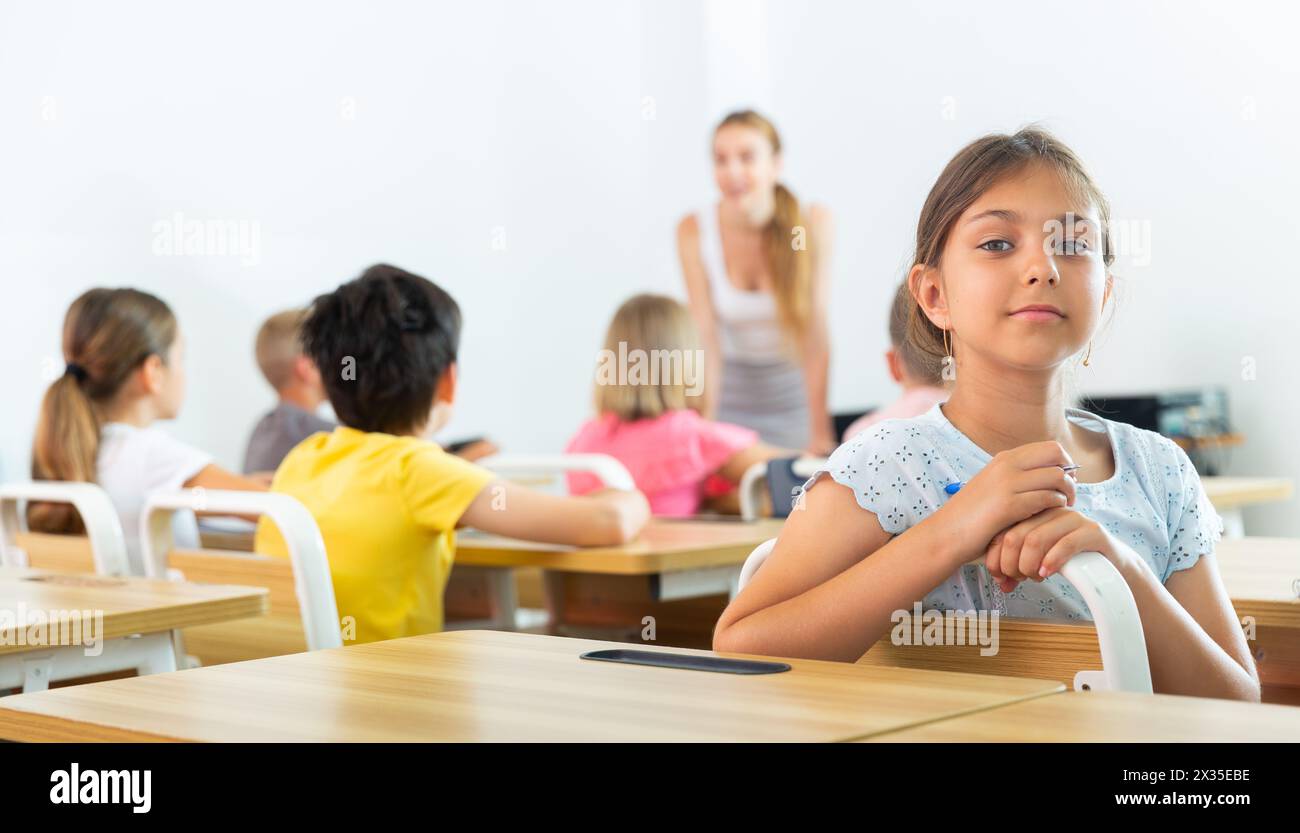 Positive tween schoolgirl sitting at school desk at lesson in class ...