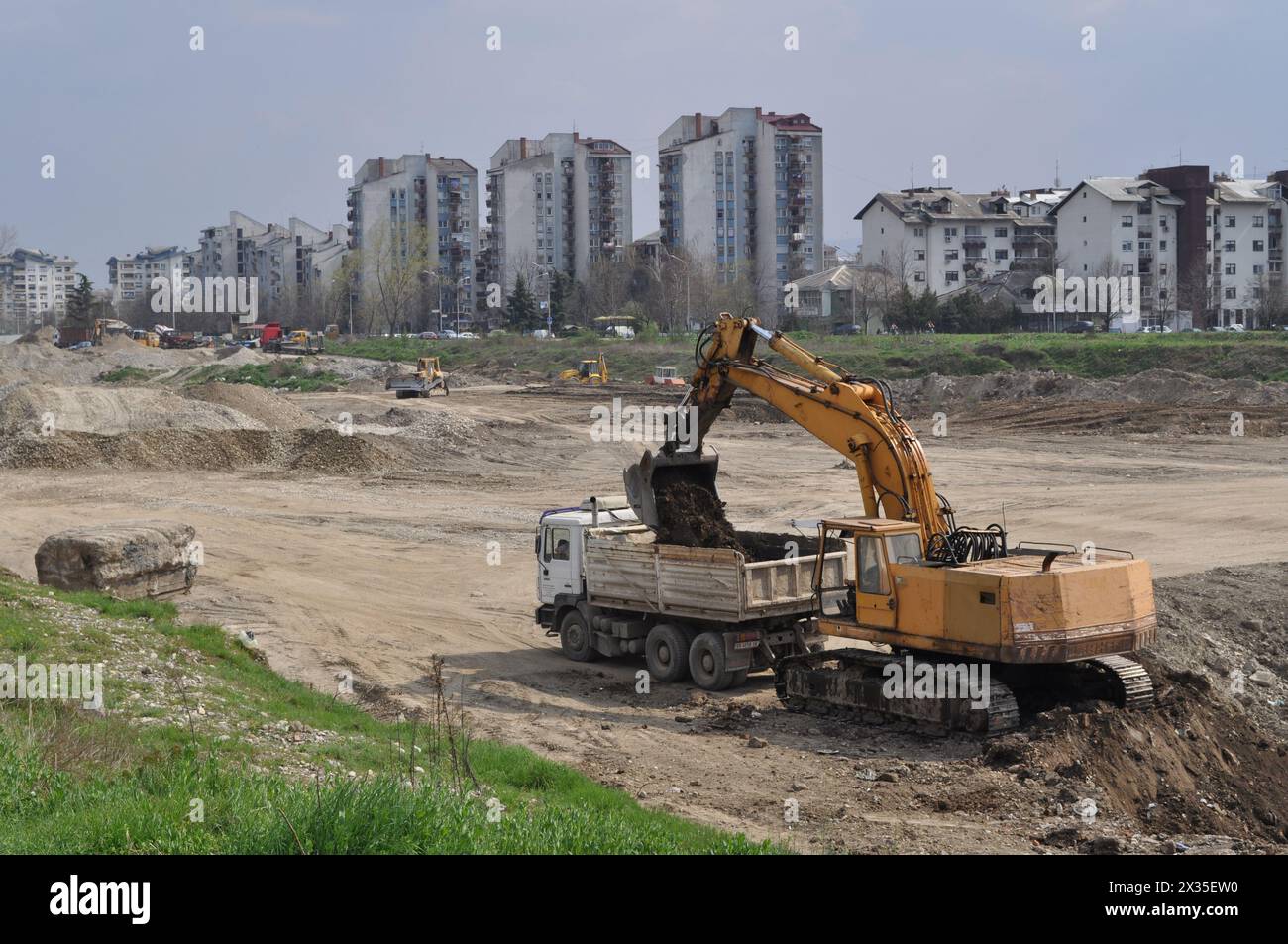 Excavator loads excavated soil into a large truck in a populated area ...