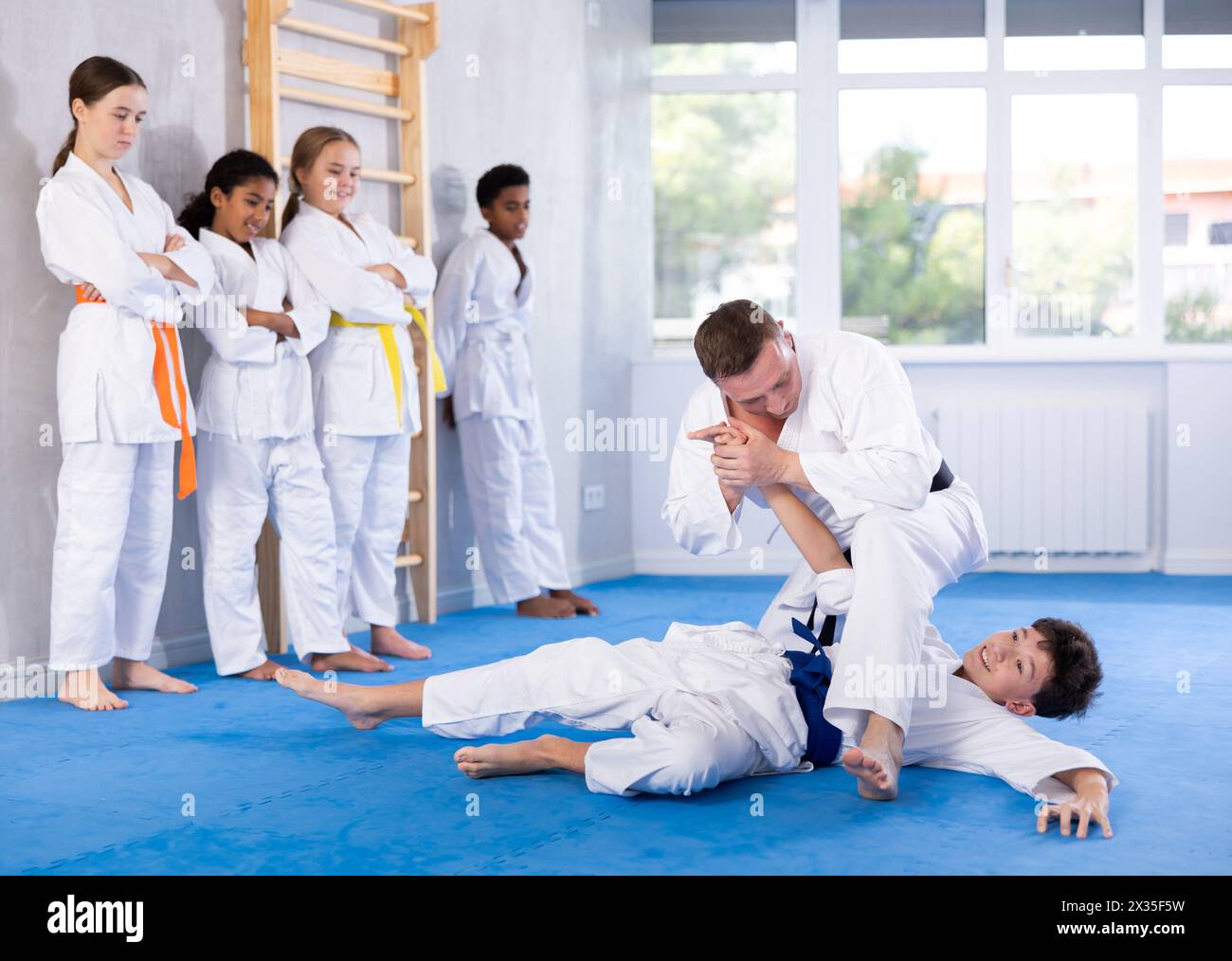 Judo coach shows fighting techniques in sparring with a boy for group ...