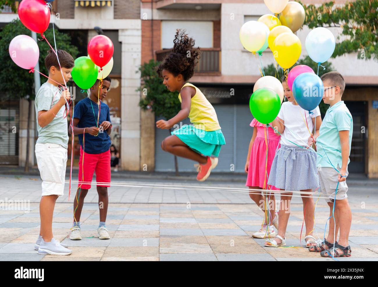 Happy preteen kids with balloons skipping on chinese jump rope in ...