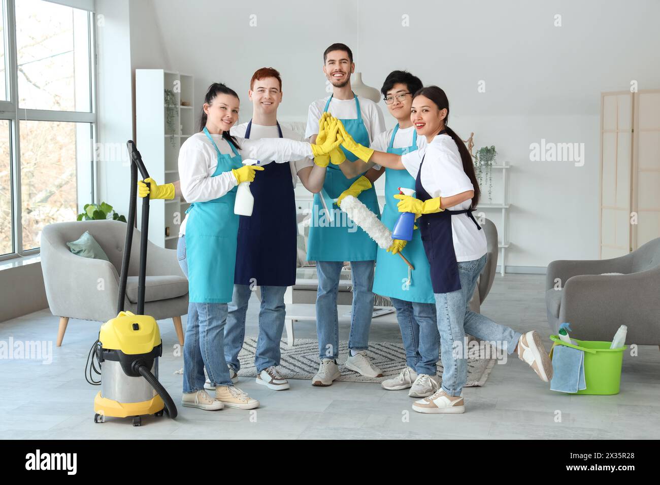 Team of young janitors with cleaning supplies putting hands together in ...