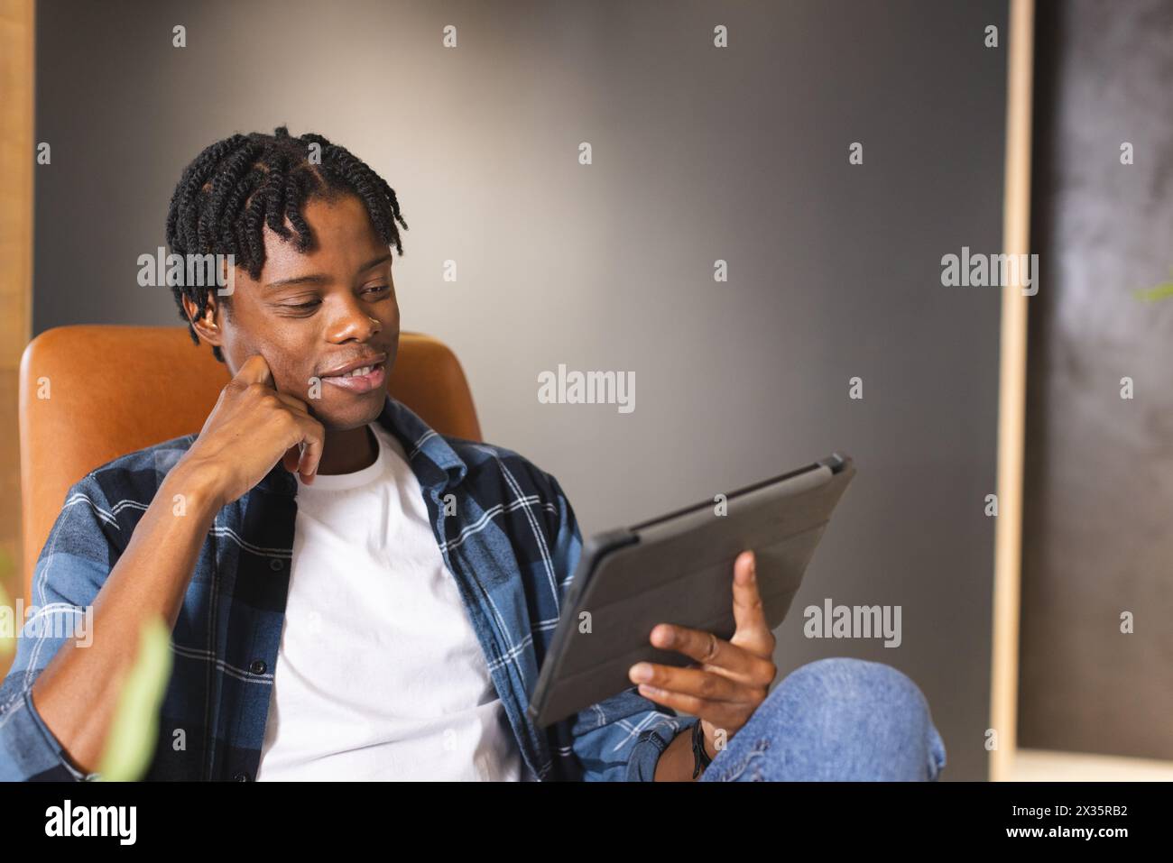 African American man holding tablet, looking at screen, sitting in a ...