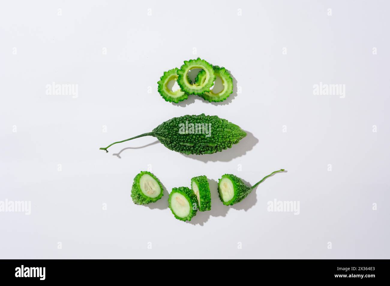 Against a white background, a fresh bitter melon and slices decorated ...