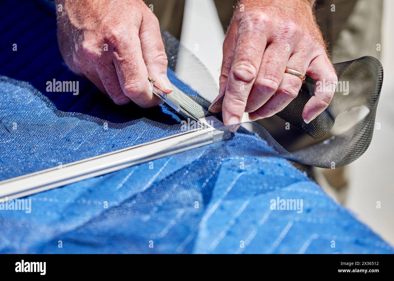 Close up the hands of a man a knife to trim a window screen in a window ...