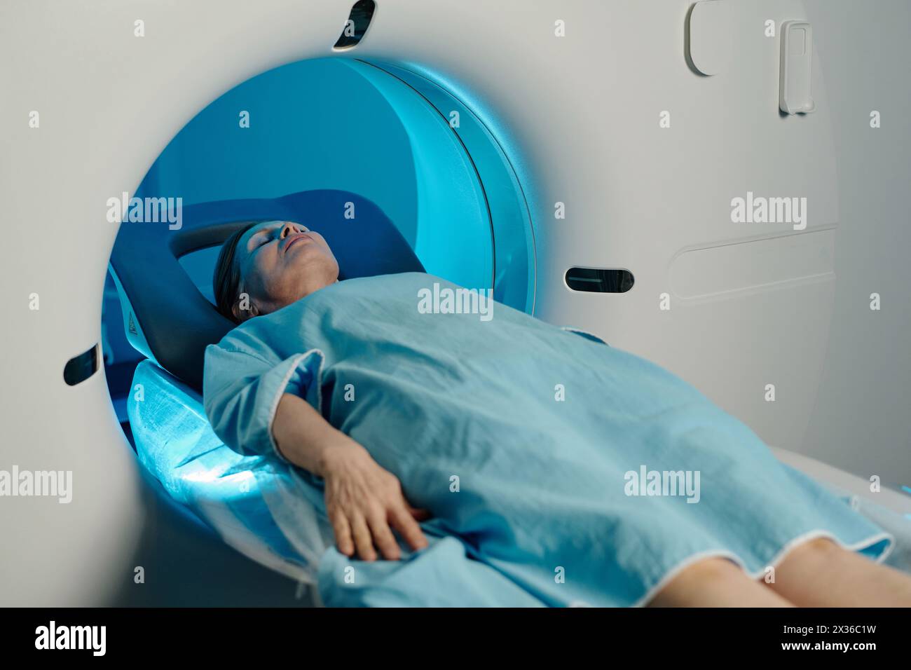 Mature Caucasian woman wearing blue gown lying on CT scanner bed having ...