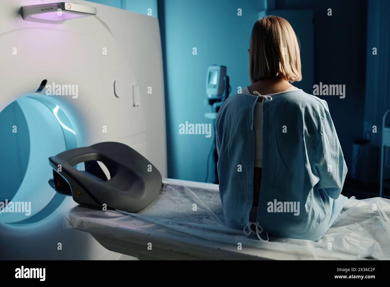 Rear view shot of unrecognizable woman wearing patient gown sitting on ...