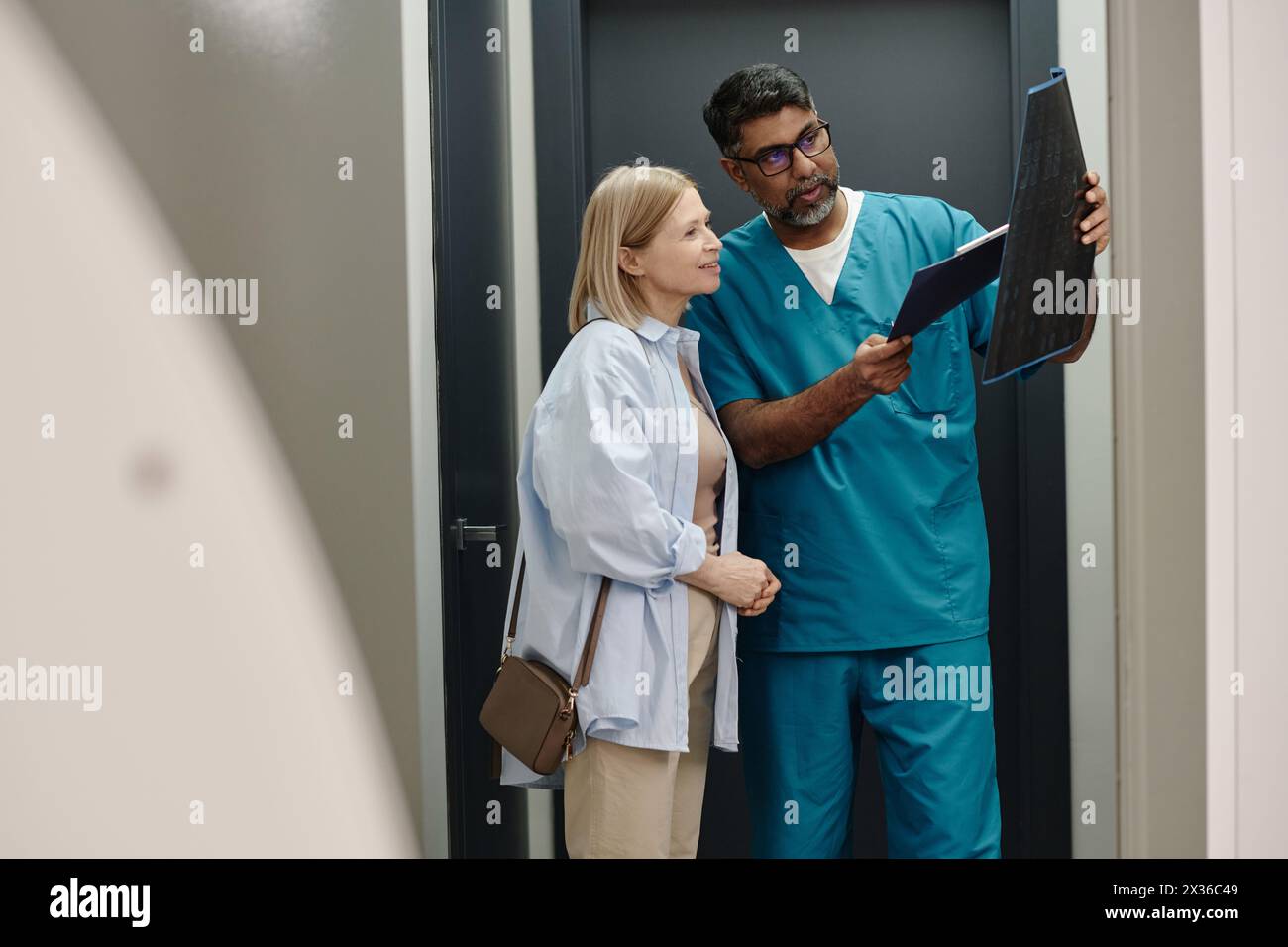 Medium long shot of biracial radiographer showing X-ray image to mature ...