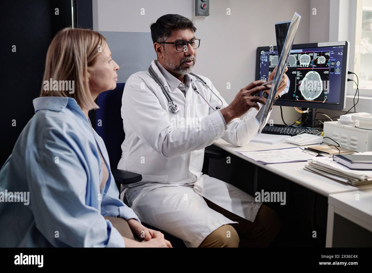Biracial radiographer showing brain X-ray image to mature Caucasian ...