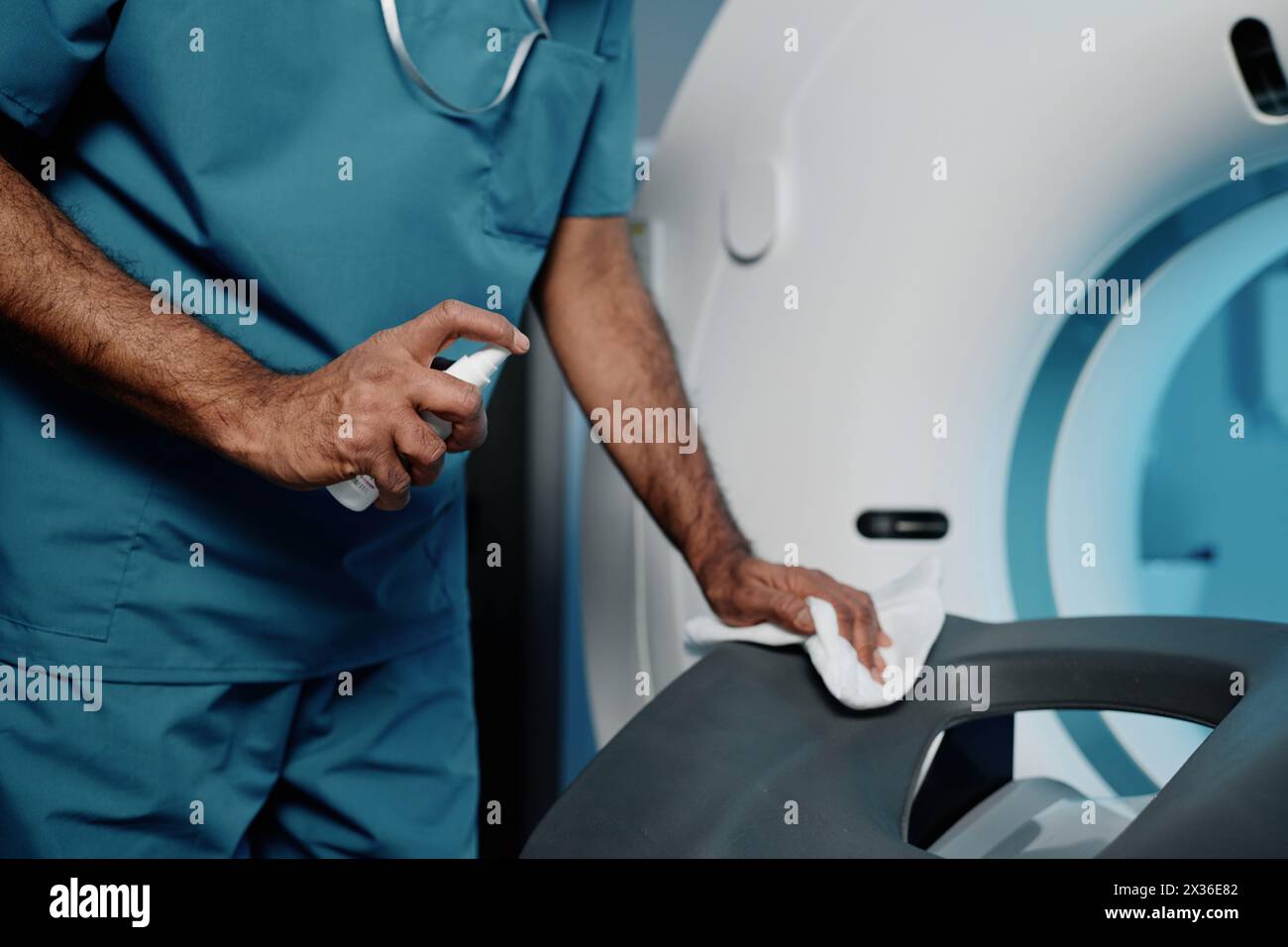 Unrecognizable male radiographer cleaning CT scanner bed with detergent ...