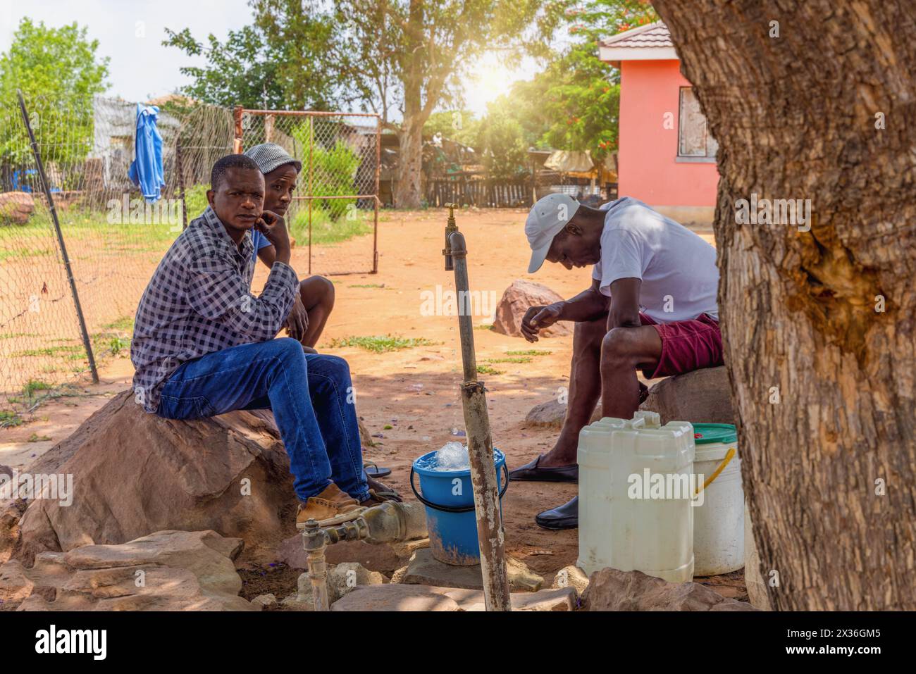 village african men neighbors sited on rocks in the yard filling ...