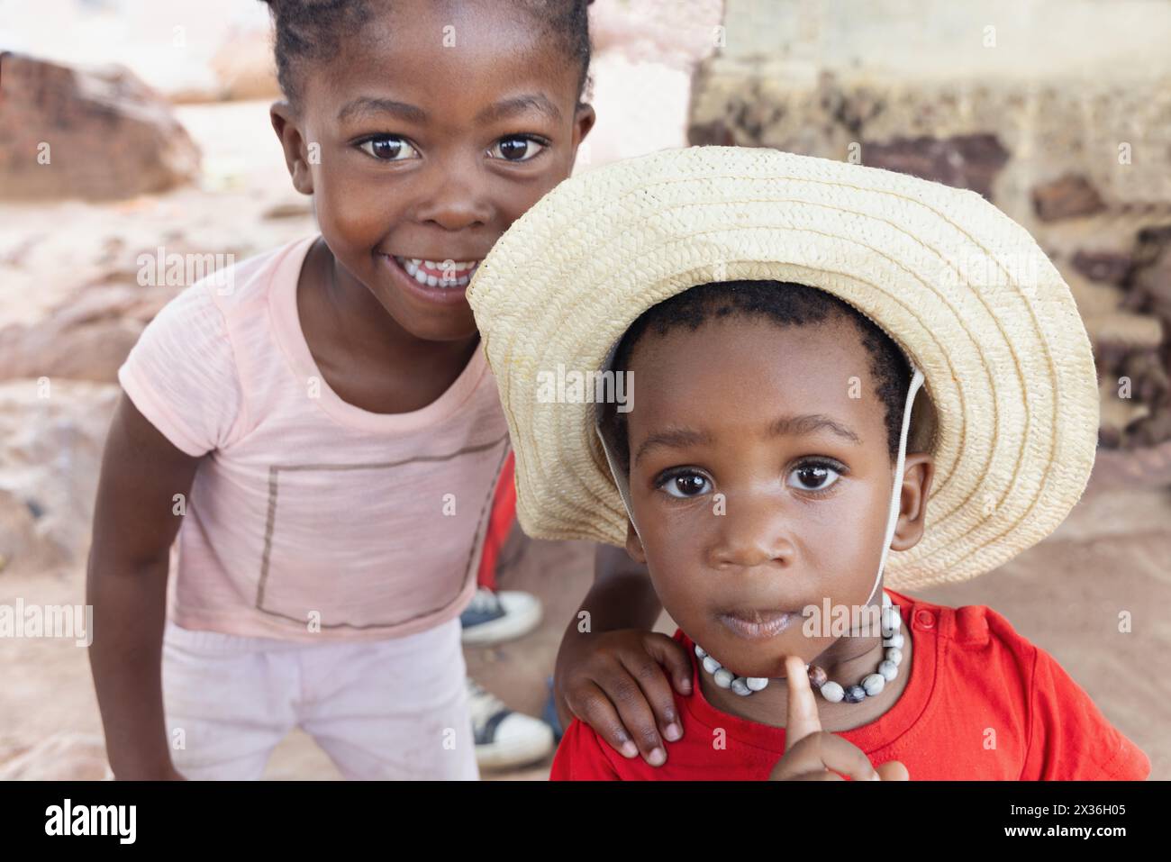 two small african kids in front of the house in the yard, wearing a red ...