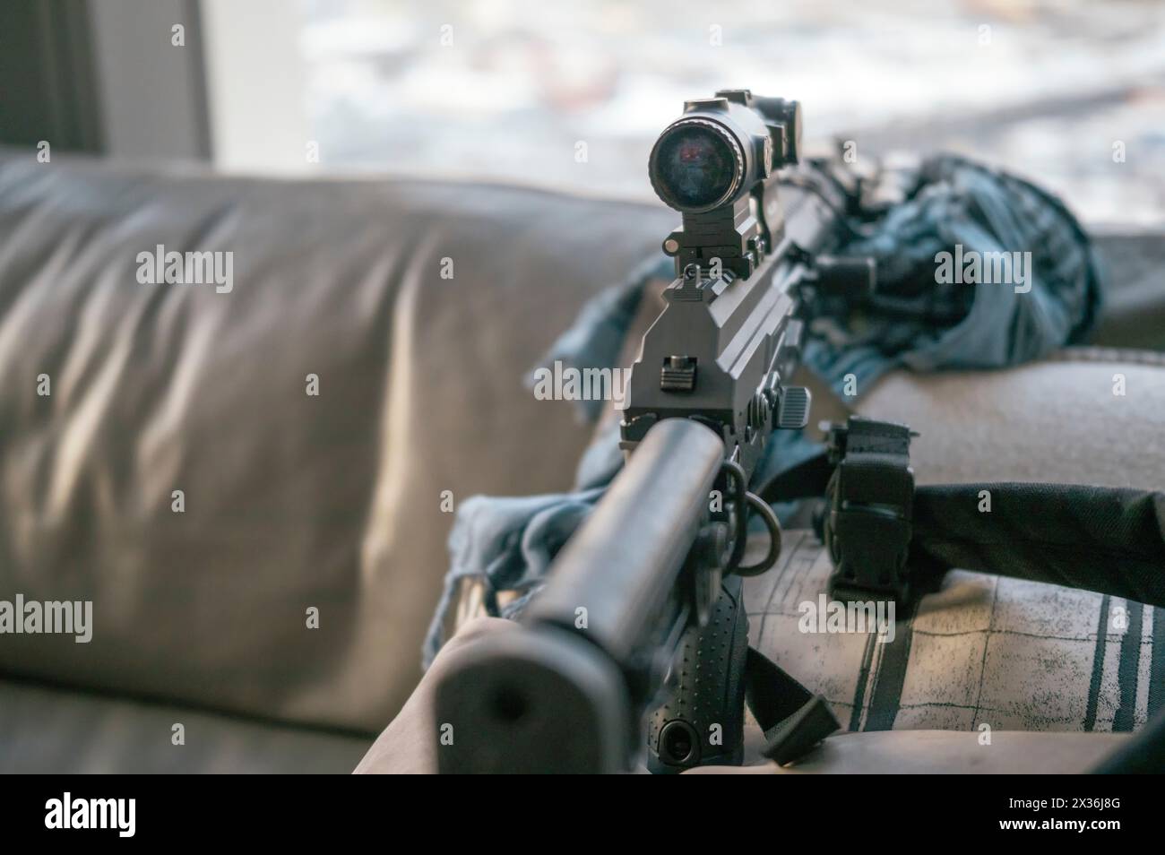 an assault rifle with optic sight on the sofa next to the window ...