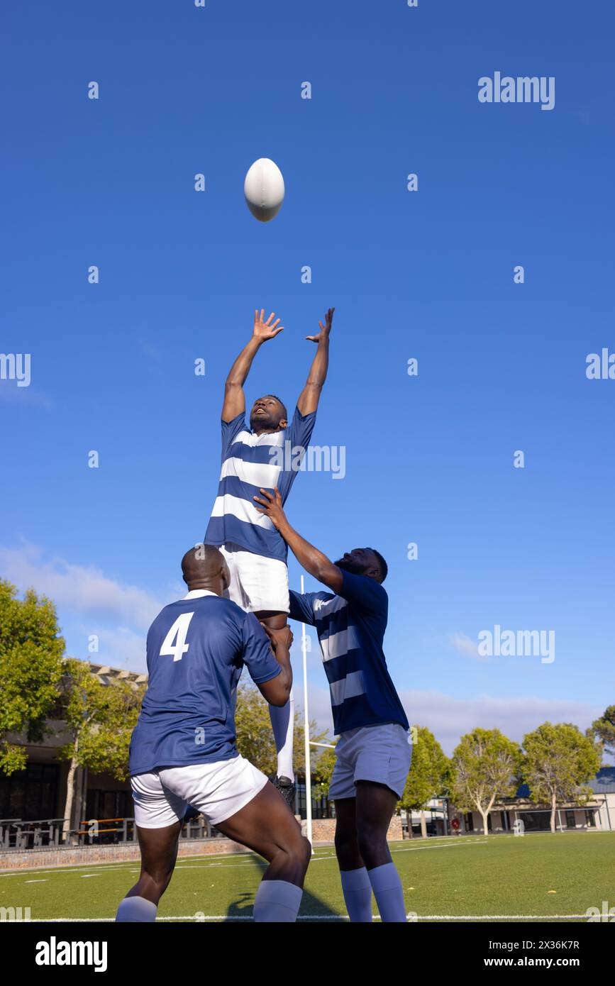 Three young African American men play rugby, one leaps for the ball ...