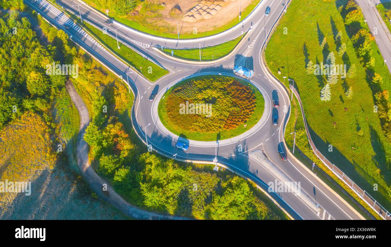 Aerial perspective of a busy roundabout with multiple exits, surrounded by lush green trees and ...