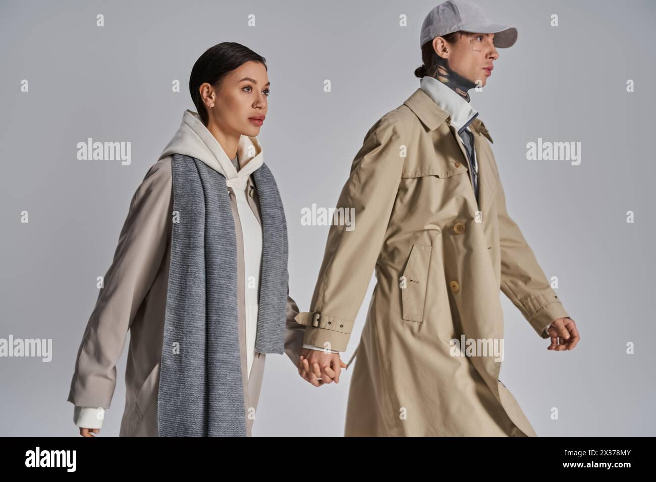 A young stylish couple in trench coats walking hand in hand, immersed ...