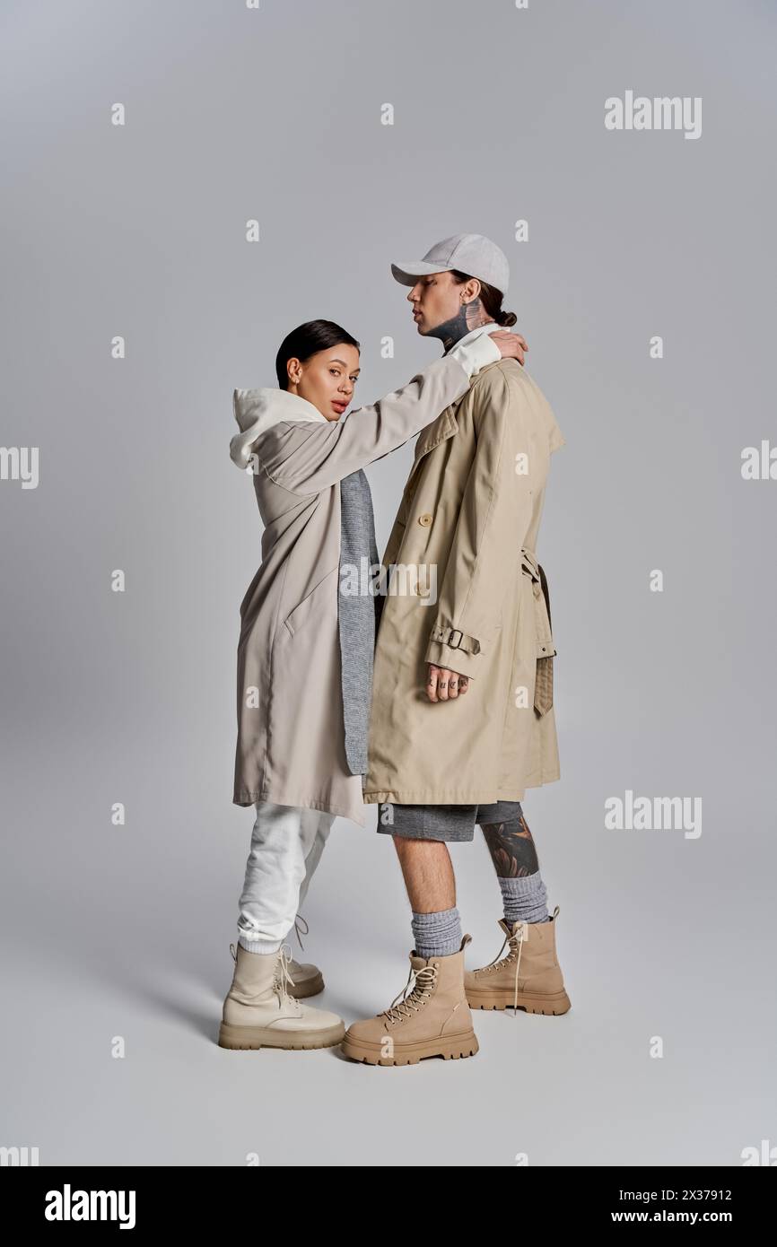 A young stylish couple in trench coats stands gracefully together in a ...