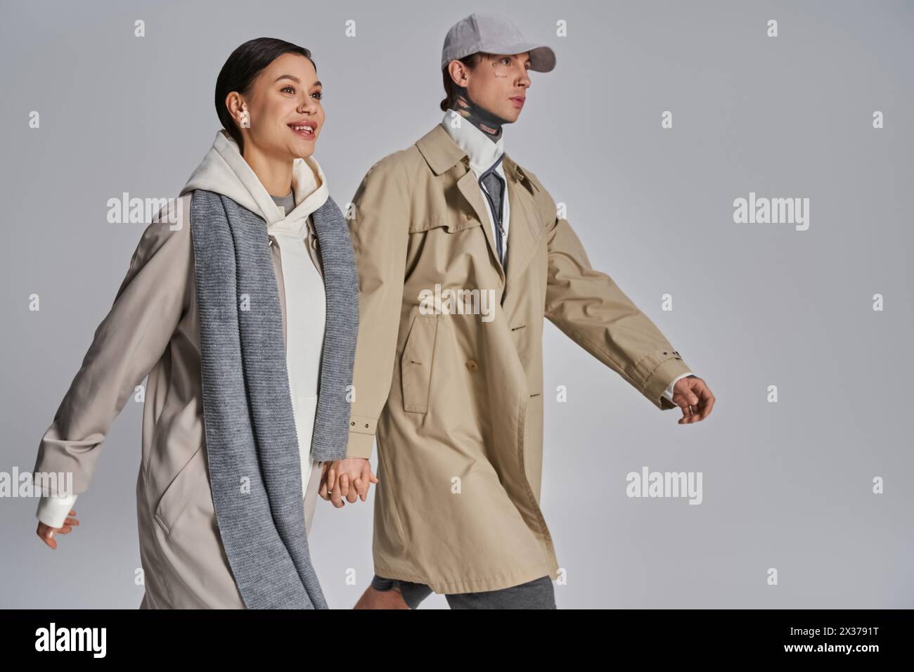 Young stylish couple in trench coats walking together in a studio ...