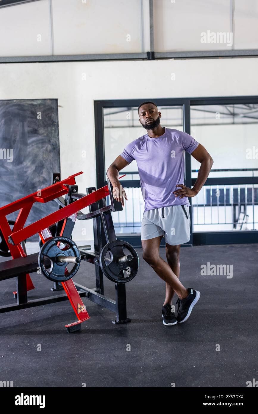 African American male athlete, fitness model, leans on gym equipment ...
