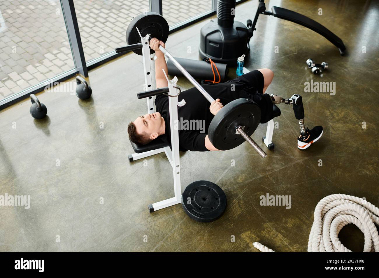 A disabled man with a prosthetic leg calmly laying on a bench in a gym ...
