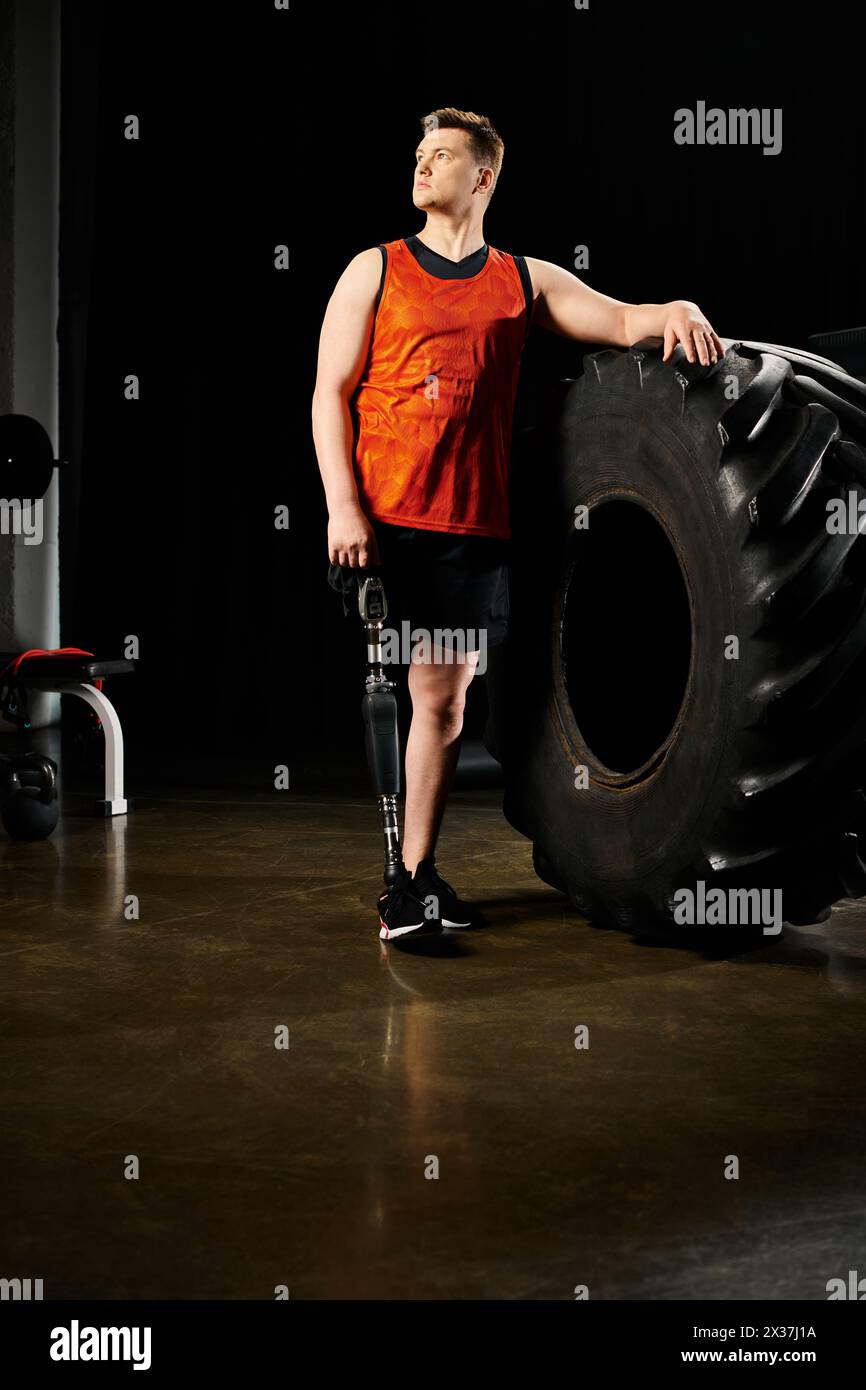 A man with a prosthetic leg standing next to a massive tire in a gym ...