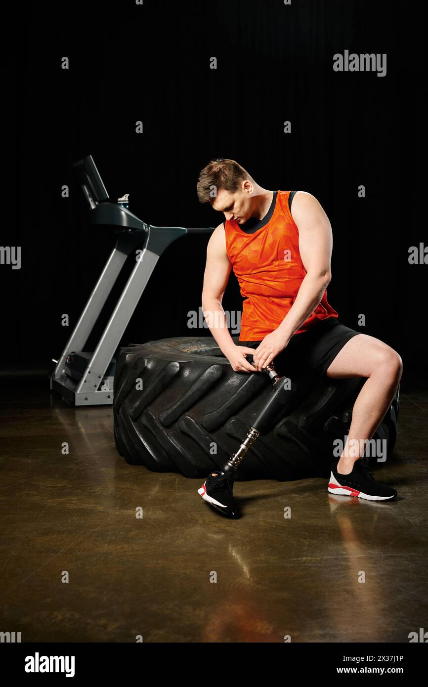 A man with a prosthetic leg sitting on top of a black tire in a gym ...