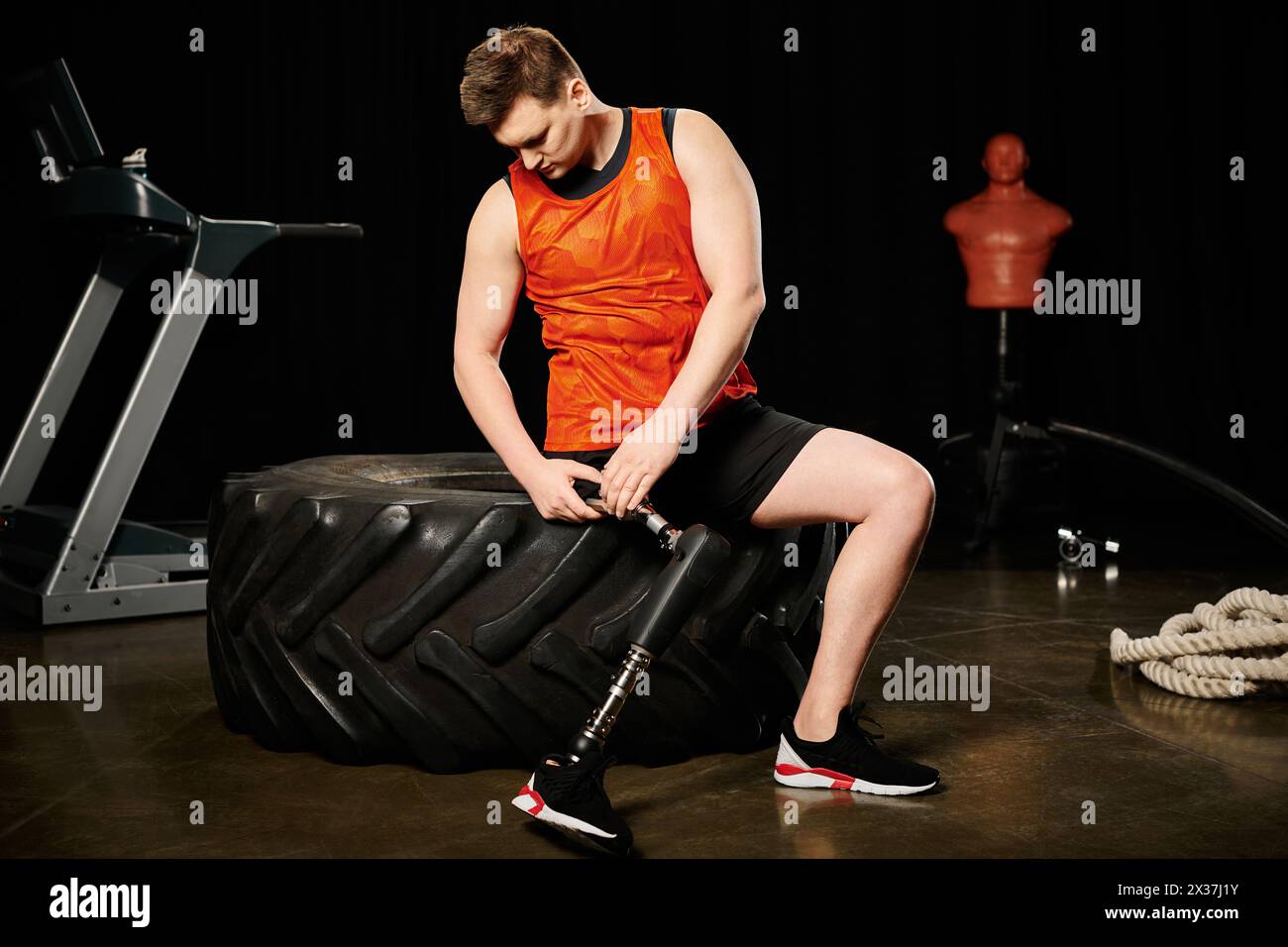 A man with a prosthetic leg sits on a tire next to a machine, deep in ...