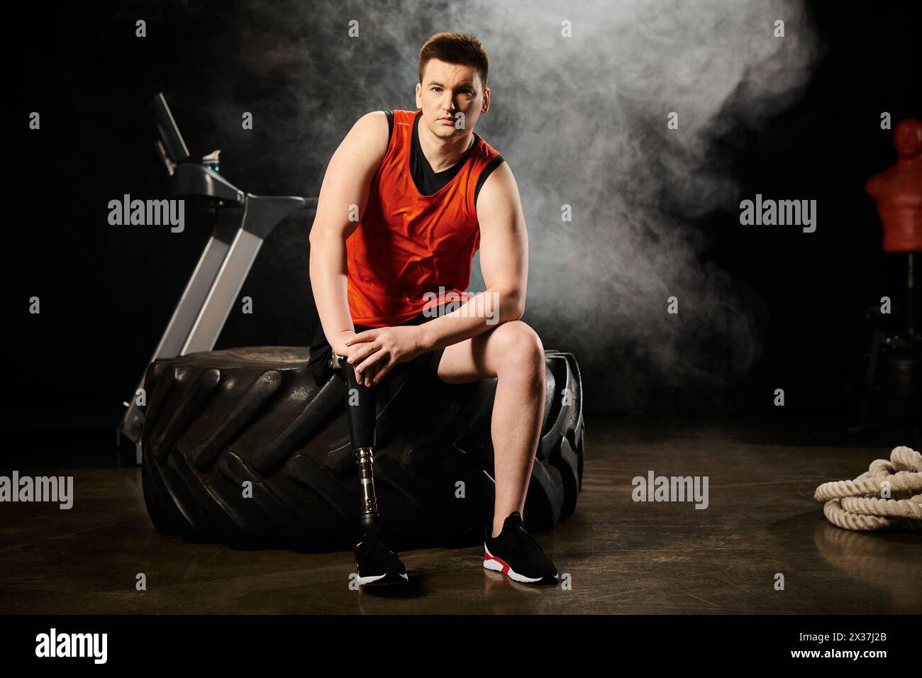 A man with a prosthetic leg sits atop a tire, in a determined pose ...