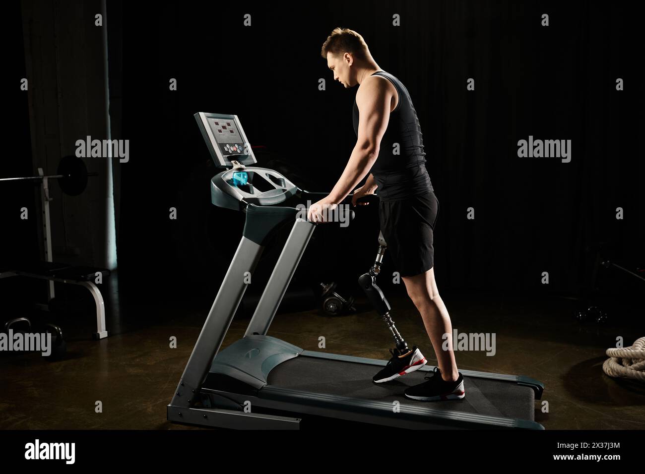 A man with a prosthetic leg exercises on a treadmill in the dimly lit ...