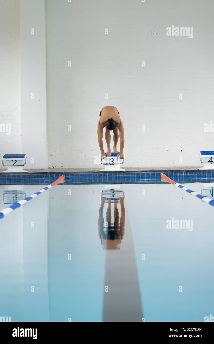 Caucasian boy in goggles readies to dive into pool from indoor starting ...