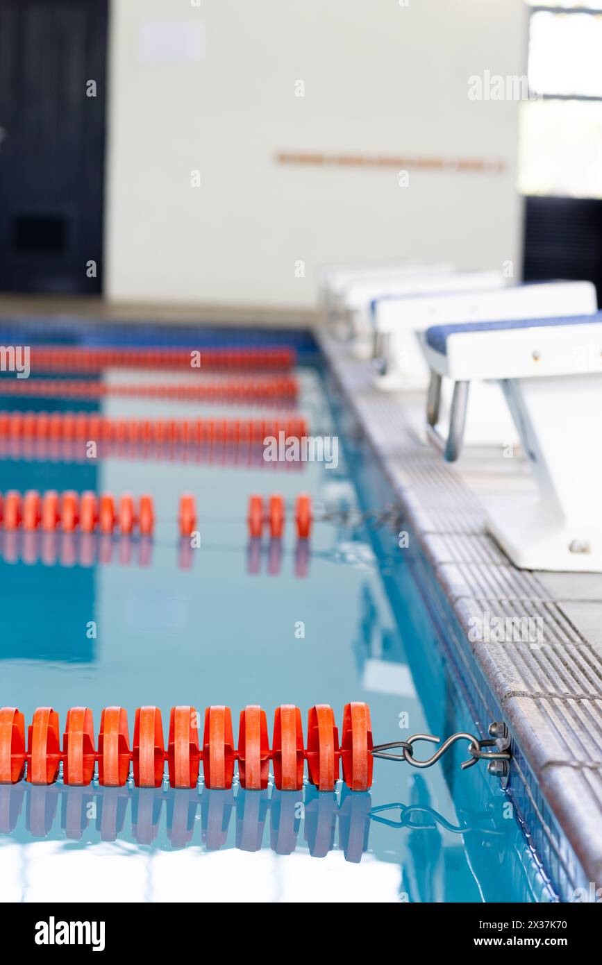 Swimmers wearing caps and goggles preparing to dive into an indoor pool ...