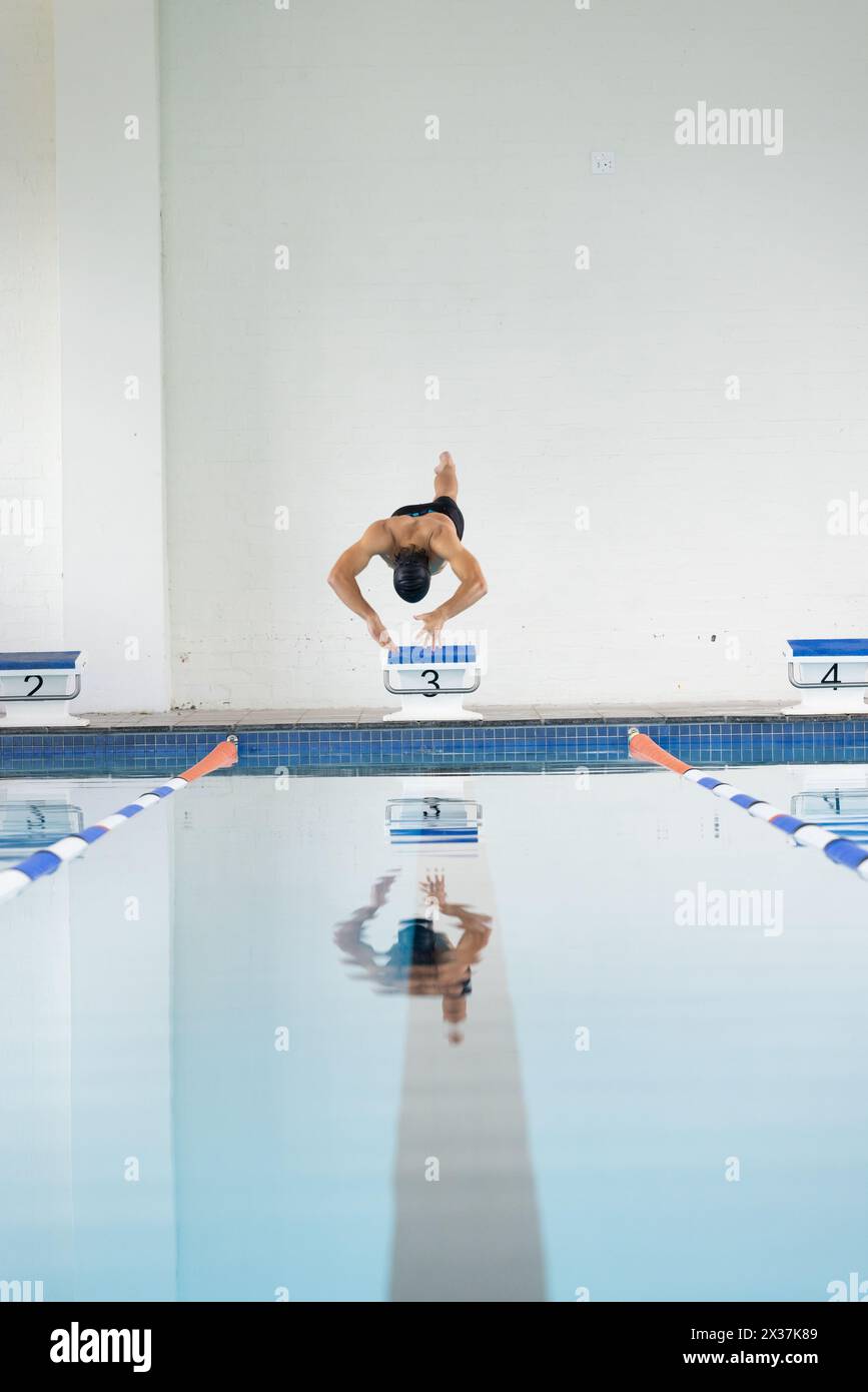 Caucasian young male swimmer diving into swimming pool from starting ...