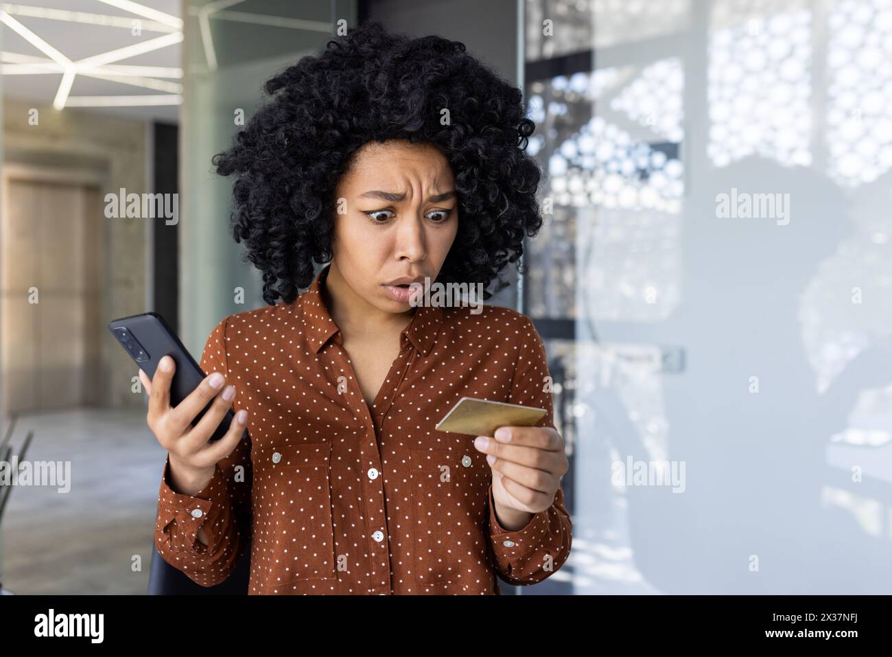 A young woman looks shocked while examining her credit card and ...