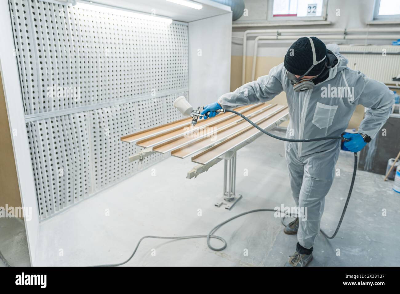 worker with safety mask painting a piece of wood with spray gun in home ...